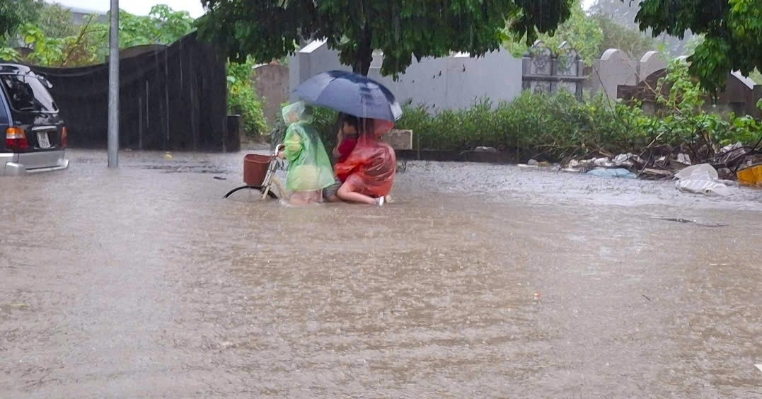 Eltern in Hanoi tragen Eimer und waten durch Wasser, um ihre Kinder von ...